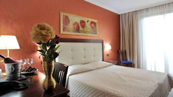 Quarto de hotel com cama, um vaso de flores, luminária e um quadro na parede.