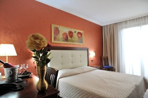 Quarto de hotel com cama, um vaso de flores, luminária e um quadro na parede.