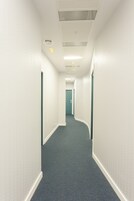 Um corredor estreito, bem iluminado, com paredes brancas e carpete escuro.