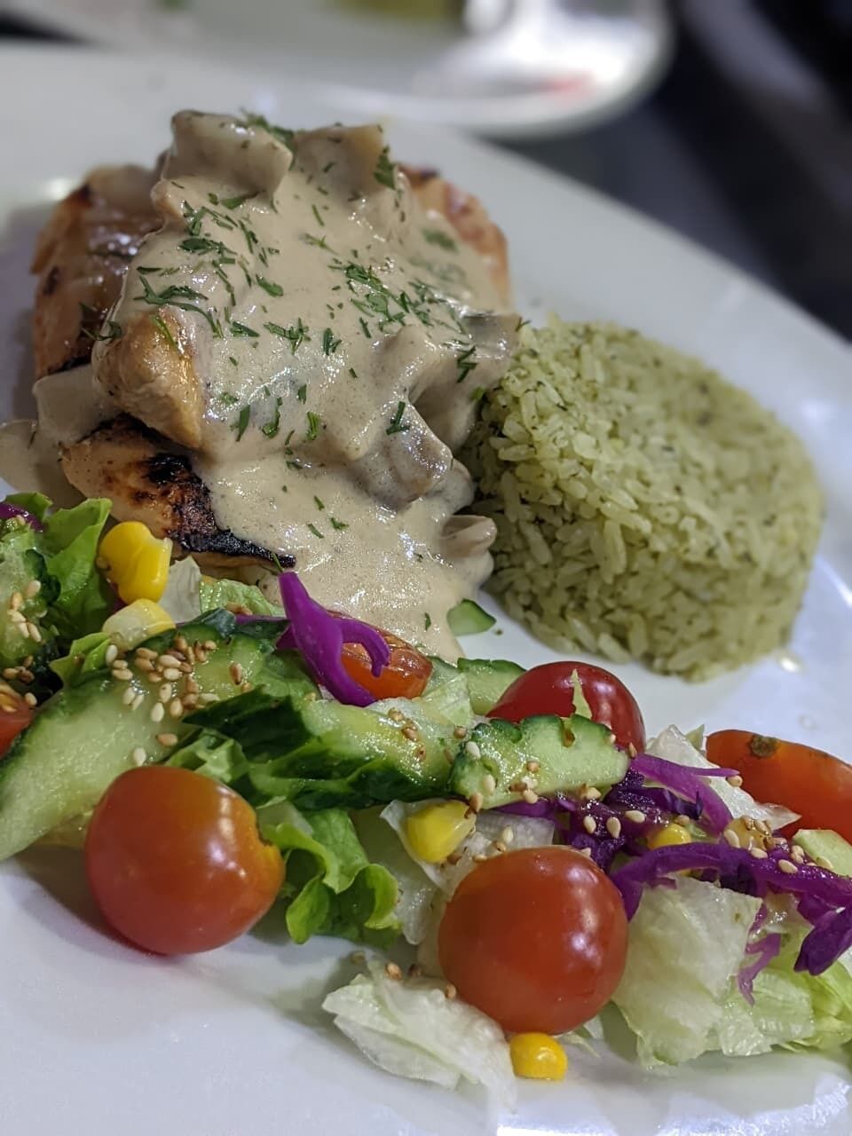 Um prato com frango grelhado, arroz e uma salada verde.