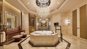 Um banheiro luxuoso com uma banheira grande e independente, um imponente candelabro e um espelho com moldura ornamentada.