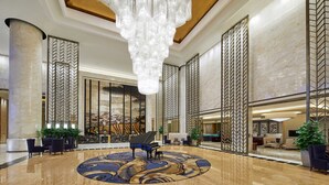 Um hall amplo com um lustre imponente, colunas de mármore e um piano.