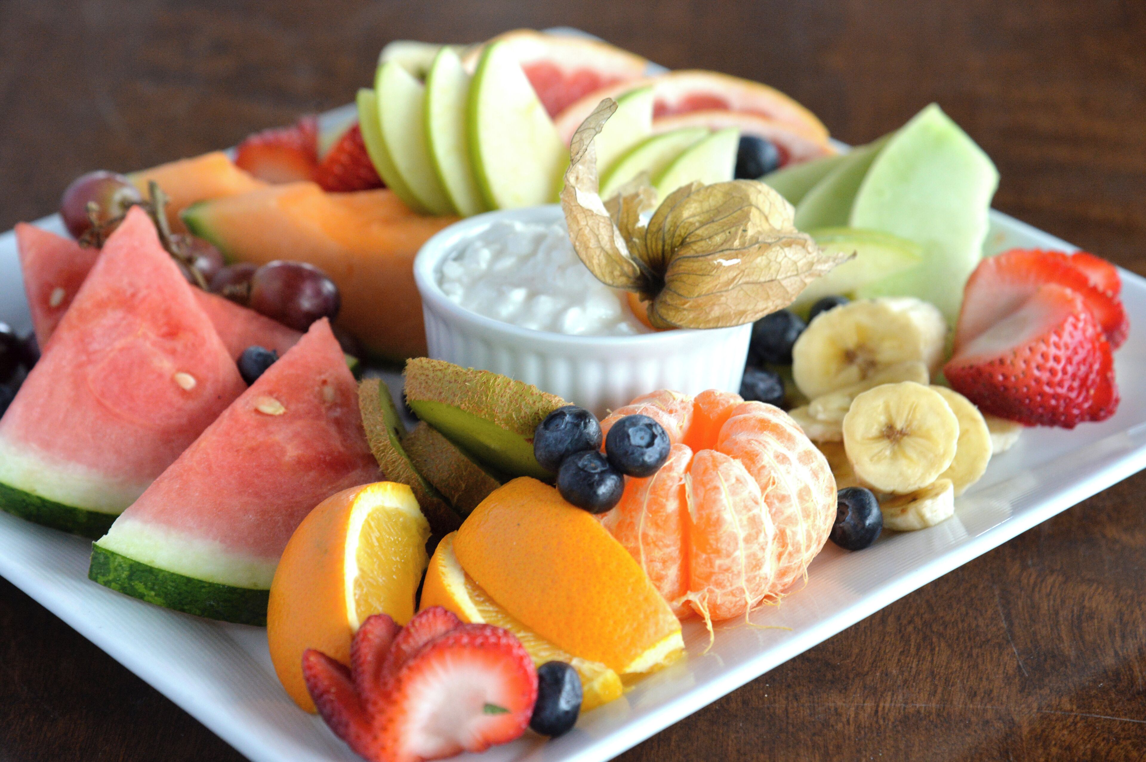 Uma travessa de frutas com diversas frutas e uma pequena tigela de iogurte.