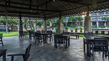 Um café ao ar livre com mesas e cadeiras, um telhado coberto e vista para a rua e edifícios.