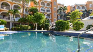 Piscina com água azul cristalina, rodeada por um hotel com várias andares, varandas e palmeiras.