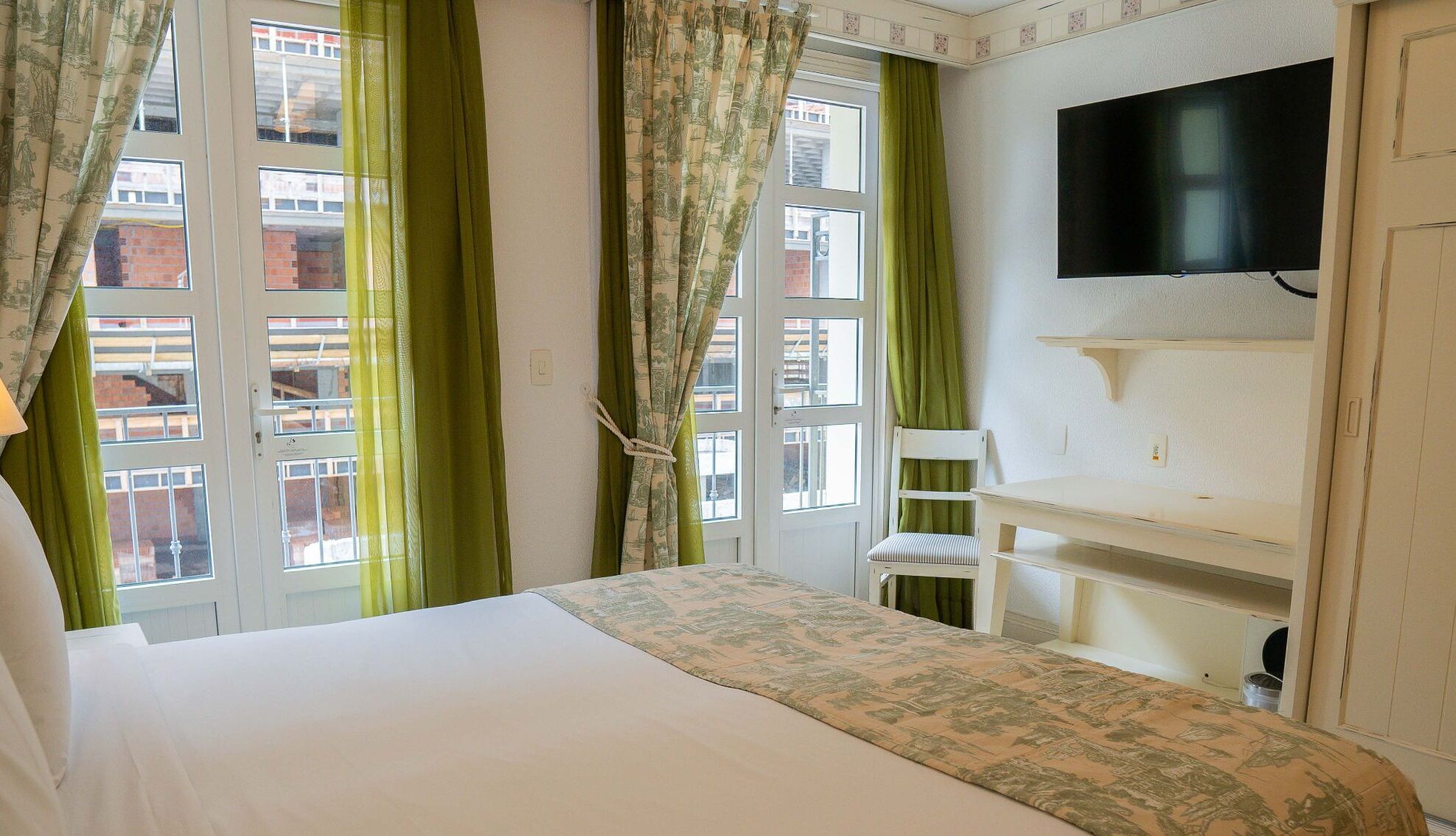 Quarto de hotel com uma cama, televisão fixada na parede e uma janela com cortinas.
