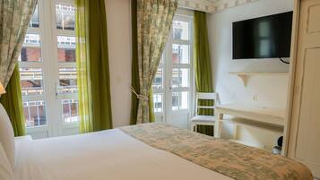 Quarto de hotel com uma cama, televisão fixada na parede e uma janela com cortinas.