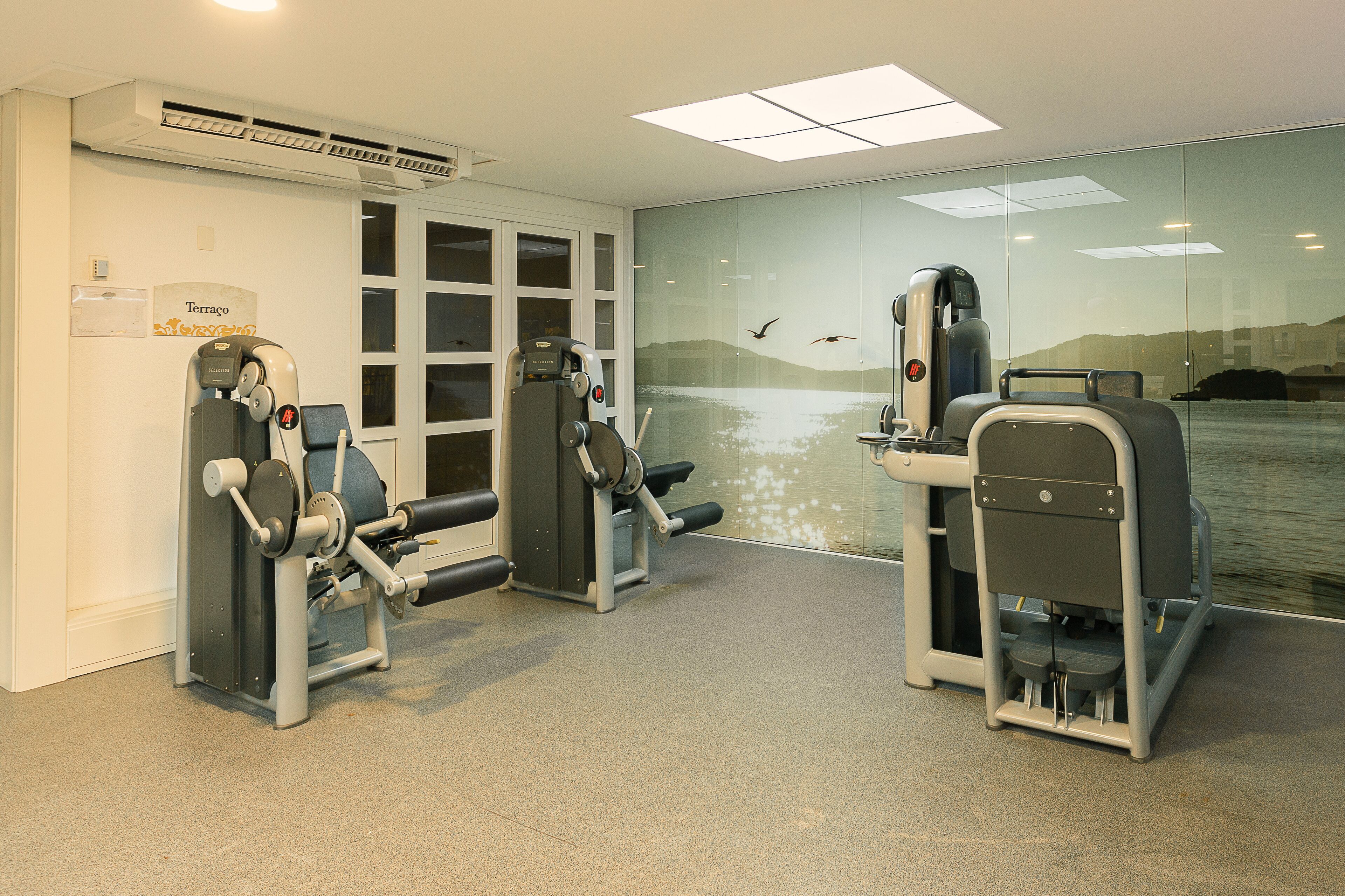 Uma academia com equipamentos de exercício, vista para a água e uma placa com a inscrição 'Terraco'.