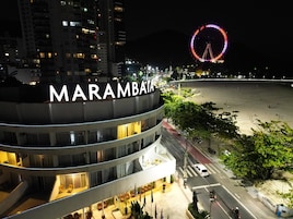 Um hotel chamado MARAMBATA com vista para uma praia e uma roda gigante ao fundo.