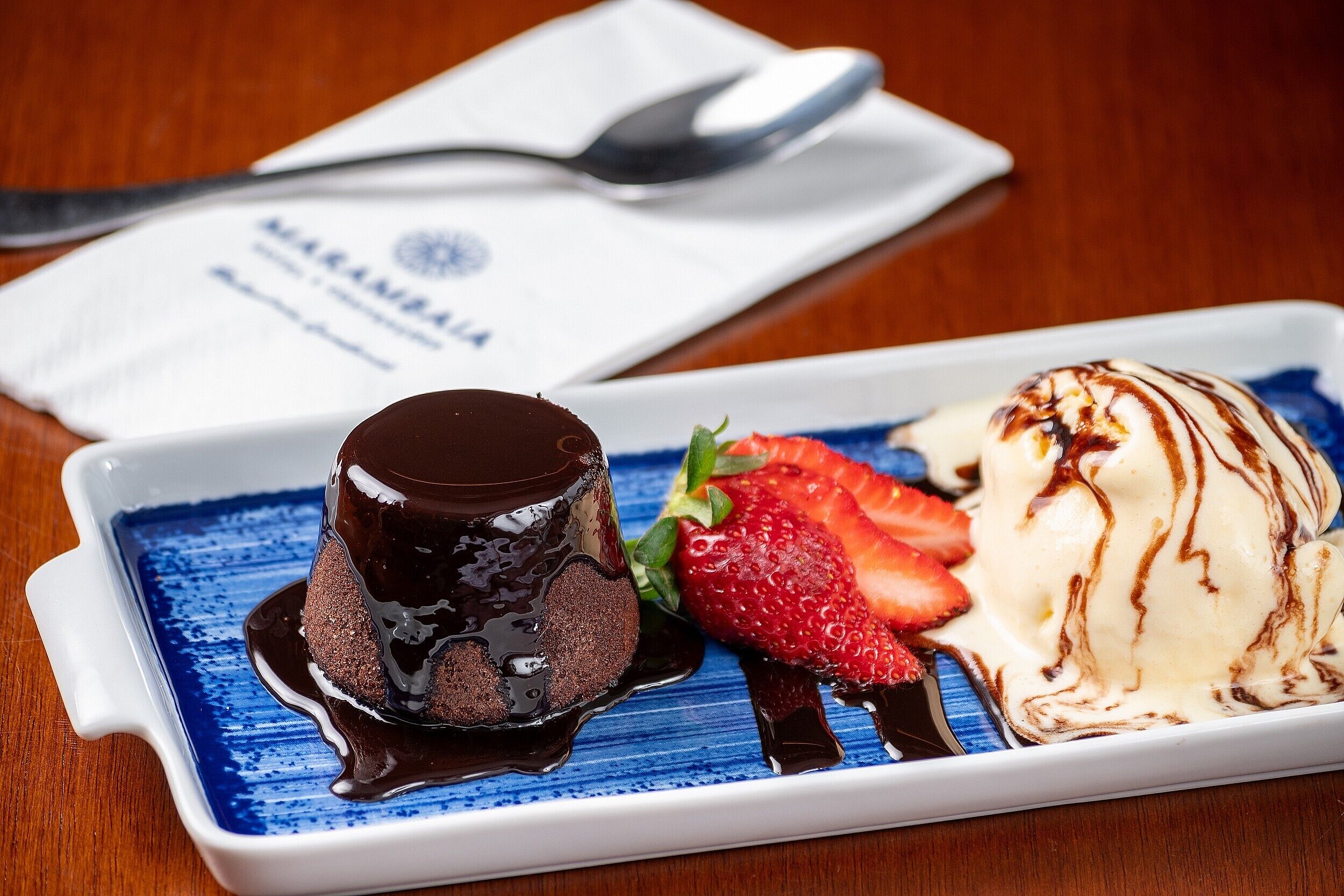 Um prato de sobremesa com bolo de lava de chocolate, morangos e sorvete com calda de chocolate.