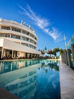 Um hotel com uma piscina grande, vários andares e bandeiras.