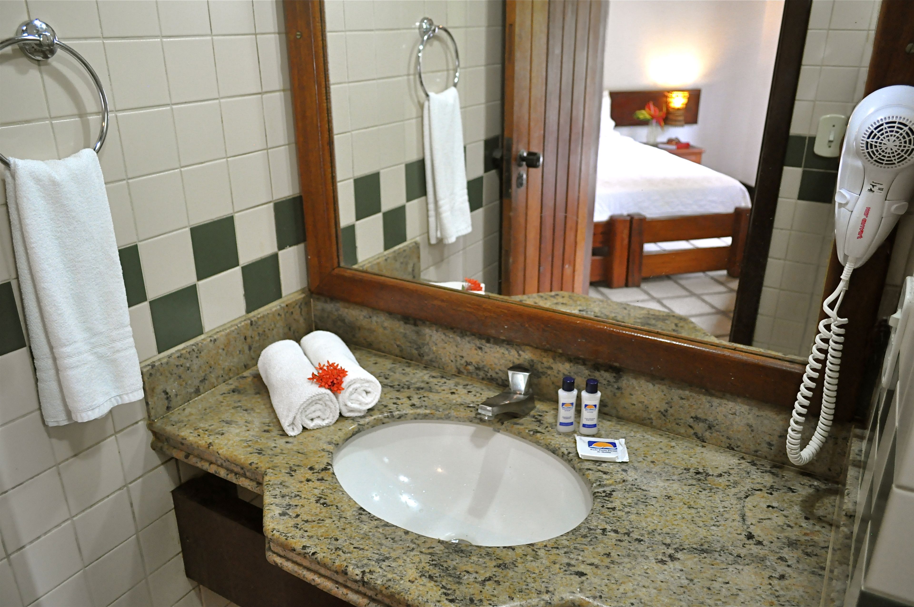 Casa de banho com bancada de granito, lavatório, espelho, secador de cabelo e toalhas.