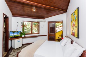 Quarto com cama, televisão, mini-frigorífico e janela com vista para palmeiras.
