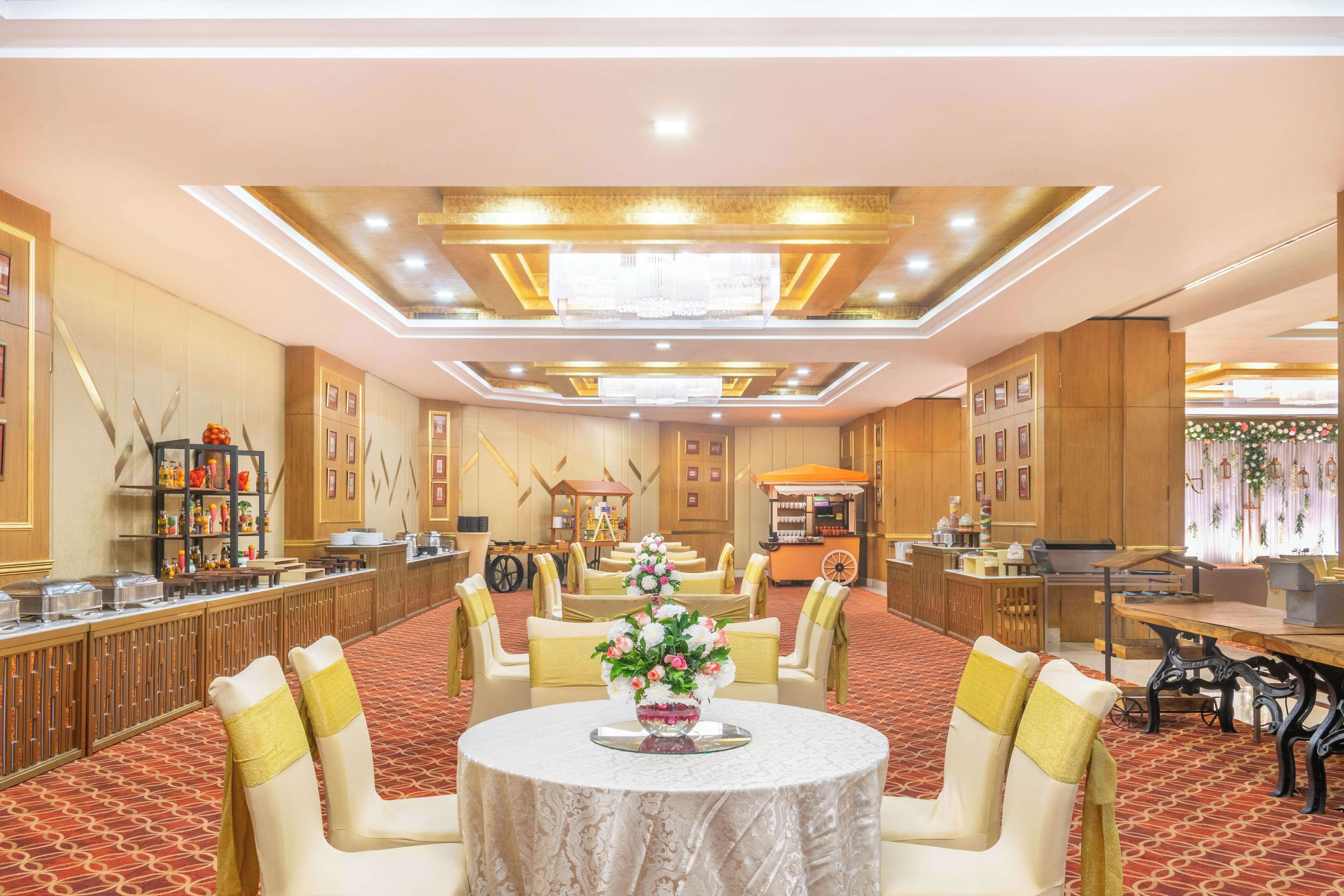 Um saguão de hotel com uma mesa redonda central, disposição de assentos, um balcão de alimentos e uma parede decorativa.