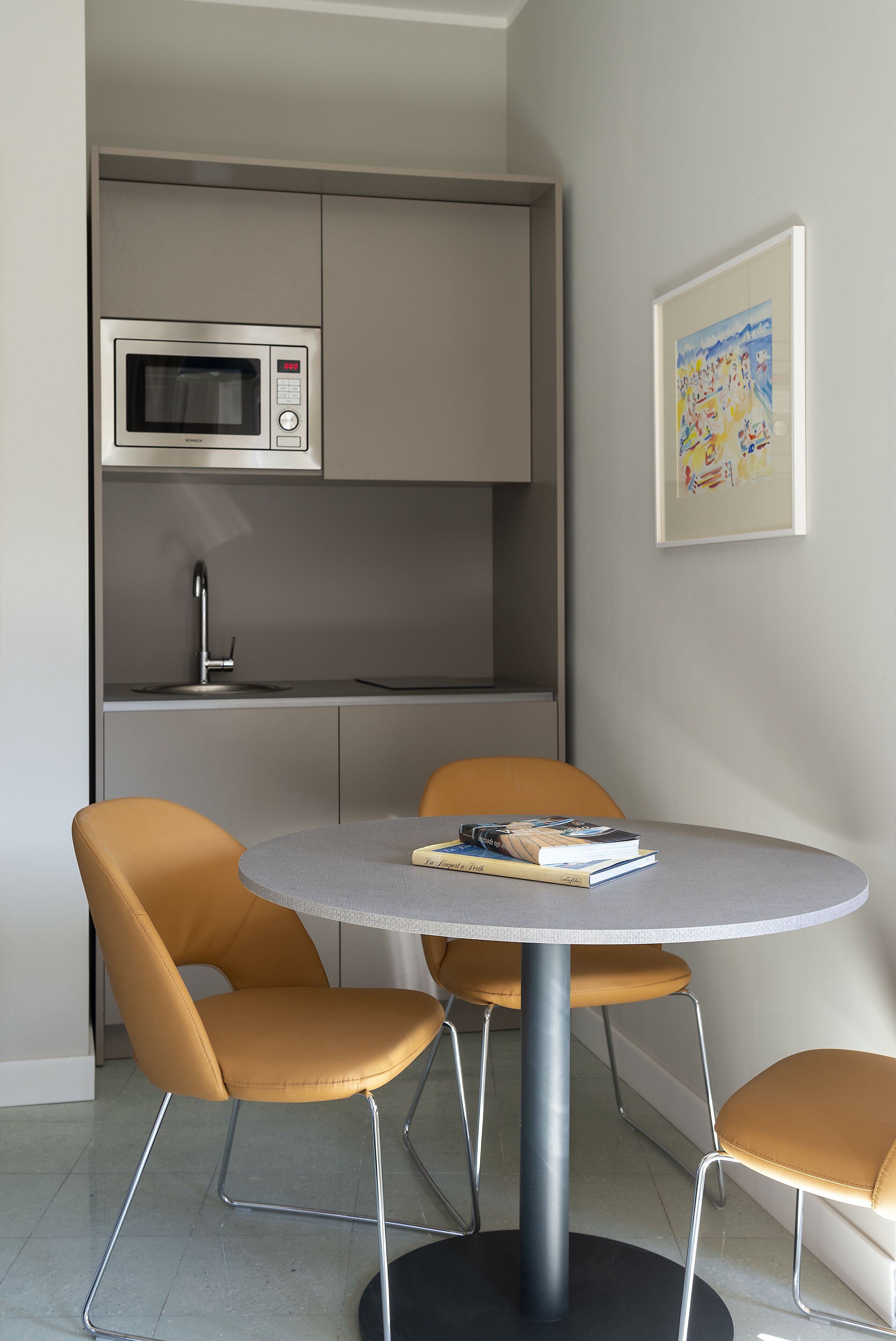 Cozinha moderna com micro-ondas embutido, pia e área de jantar com duas cadeiras e uma mesa.