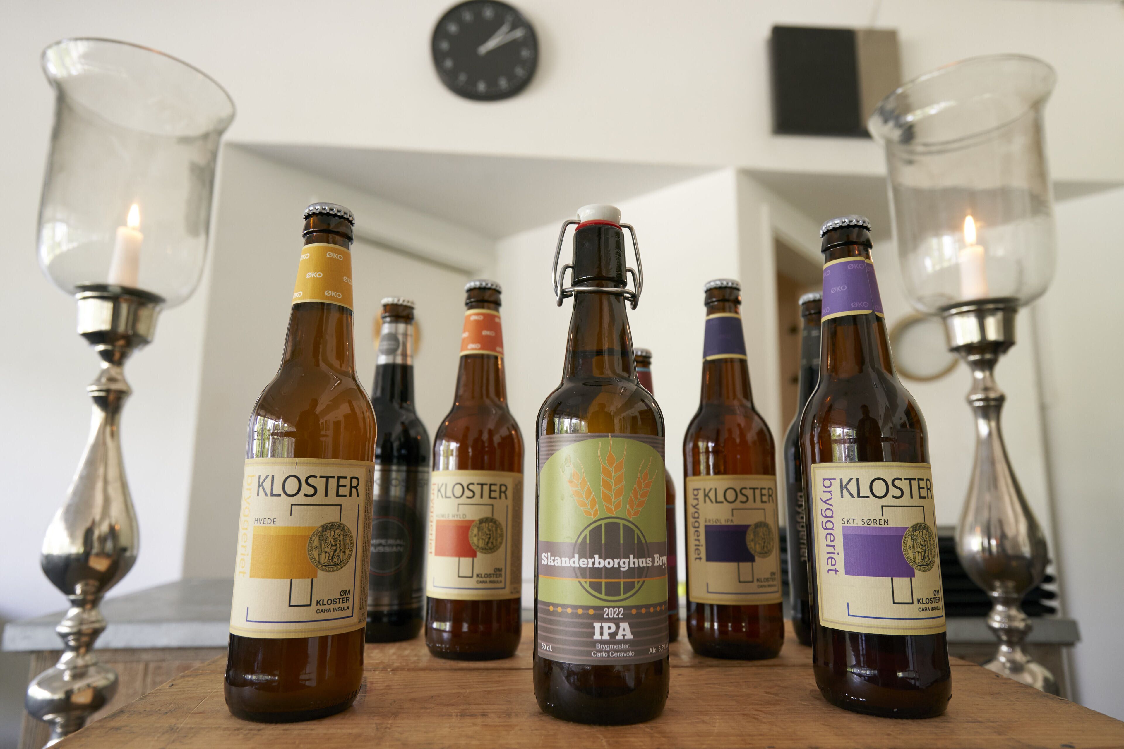Várias garrafas de cerveja Kloster sobre uma superfície de madeira, com velas em castiçais.