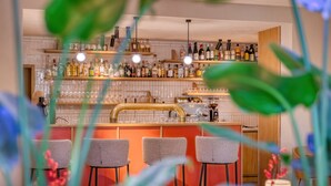 Uma área de bar com prateleiras cheias de garrafas e copos, um balcão e três banquetas.