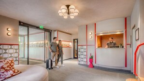 Um saguão de hotel com balcão de recepção, área de estar e porta de vidro que dá para o exterior.