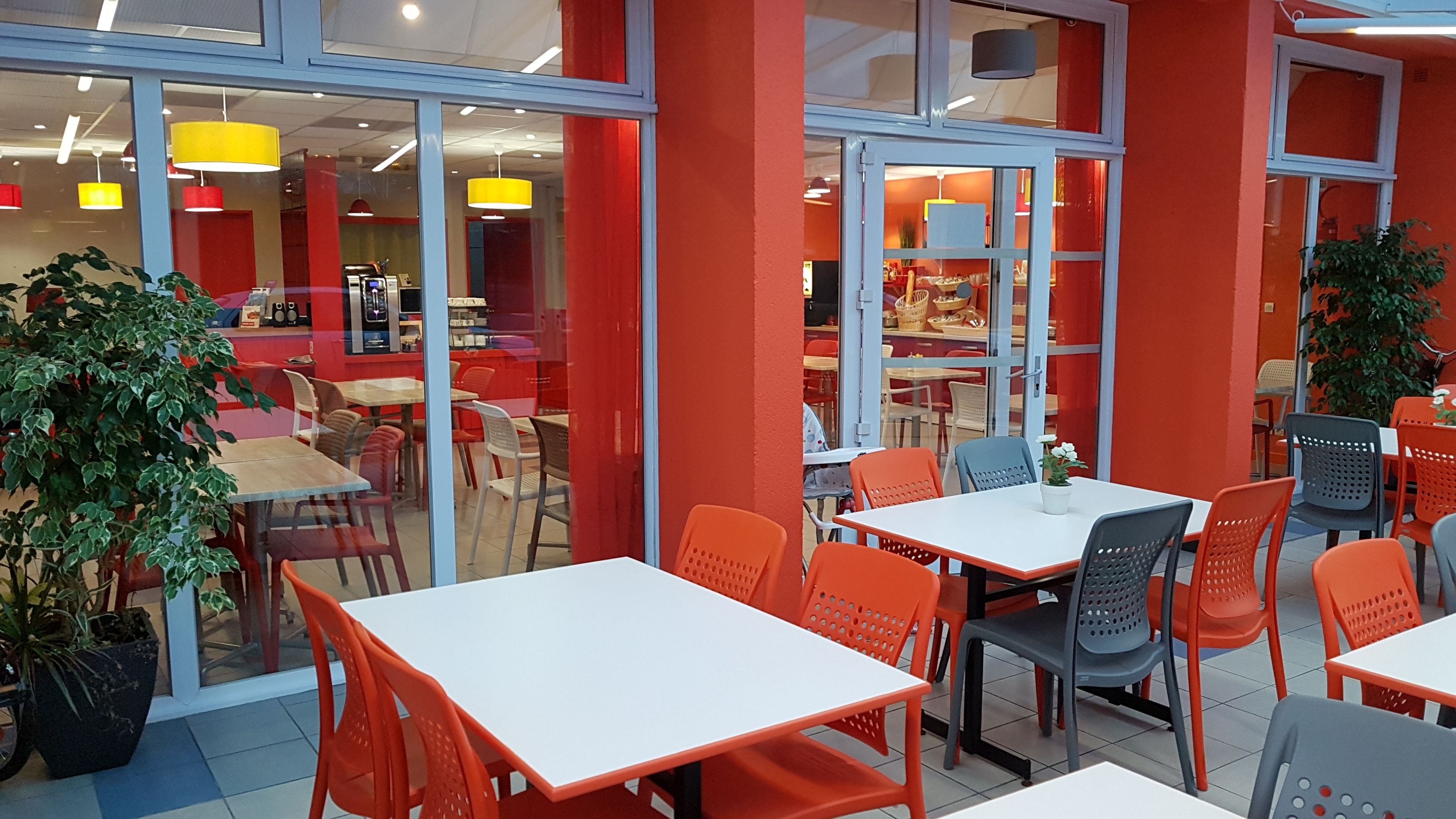 Restaurante moderno com esquema de cores vermelho e branco, divisórias de vidro e assentos internos com cadeiras laranja.