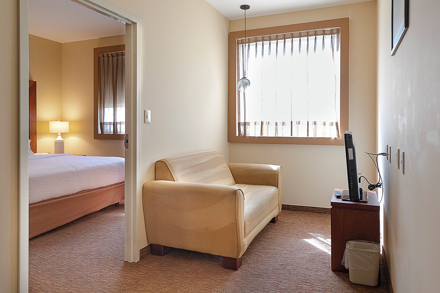 Quarto de hotel com cama, sofá, secretária com computador e janela com persianas.