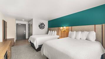 Quarto de hotel com duas camas, uma escrivaninha de madeira, um relógio de parede e uma parede de destaque em tom verde-água.