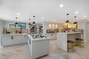 Uma cozinha espaçosa com armários brancos, uma ilha central, luminárias pendentes e um espaço de bar com banquetas.