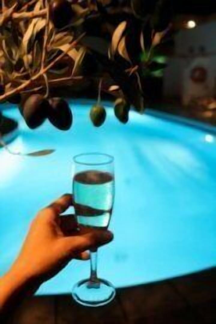 Uma mão segurando um copo d'água perto de uma piscina, com uma planta acima.