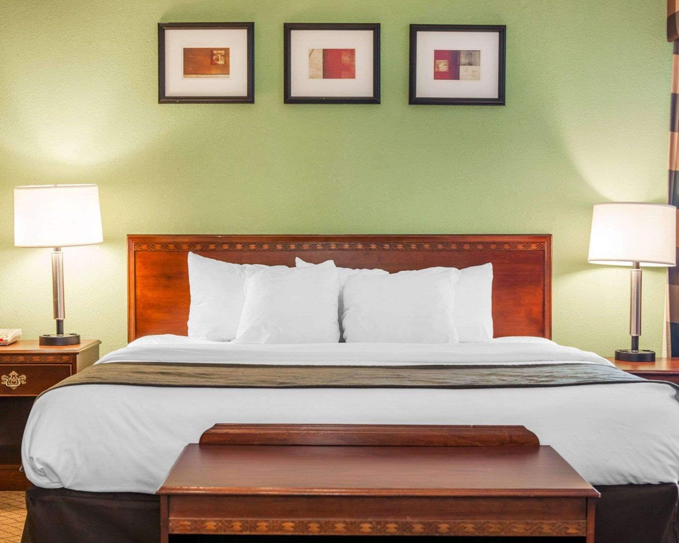 Quarto de hotel com cabeceira de madeira, roupa de cama branca e três quadros emoldurados na parede.