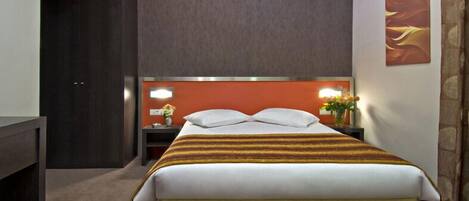 Quarto de hotel com uma cama grande, mesa de cabeceira com abajur e um quadro na parede.
