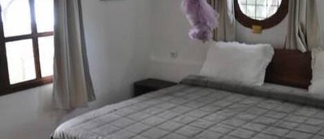 Quarto com cama, janela com cortinas, mesa de cabeceira e mosquiteiro suspenso.