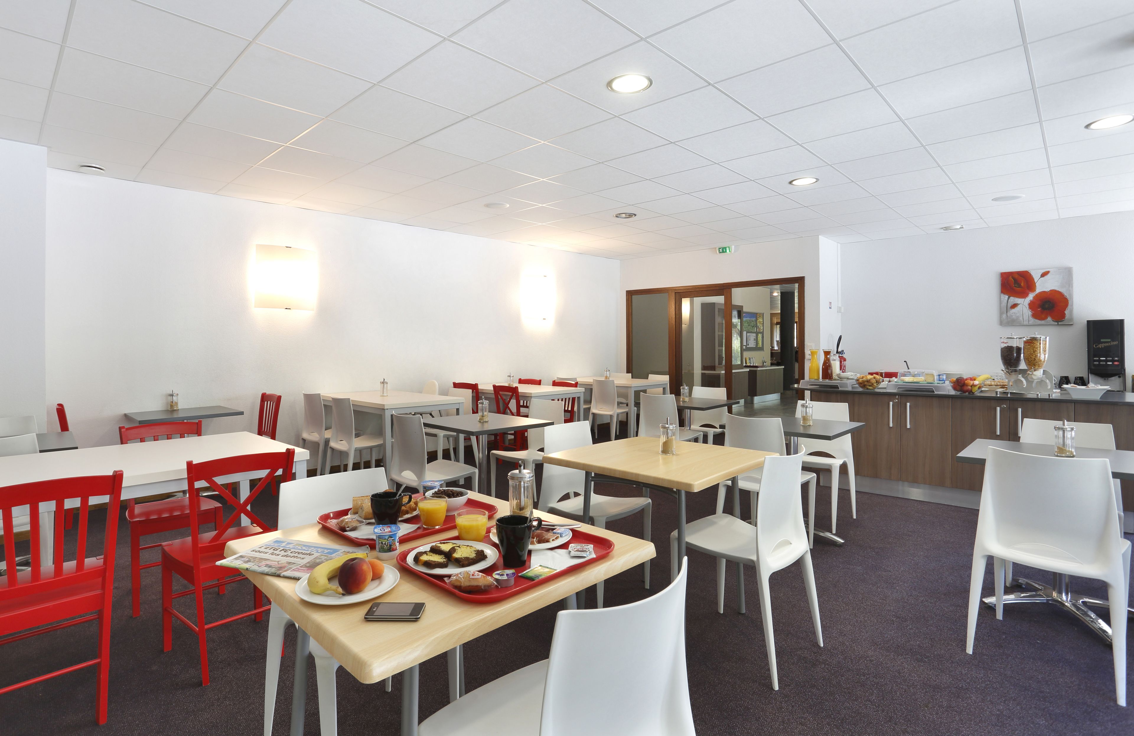 Uma área de refeições moderna com várias mesas e cadeiras, cozinha e um balcão com diversos alimentos.