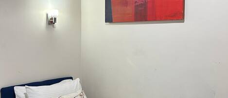 Quarto de hotel com cama bem arrumada, luminária fixada na parede e pintura abstrata colorida.