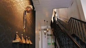 Uma escadaria com balaústres pretos e corrimão, que leva a um patamar com parede estampada e uma estátua de Buda.