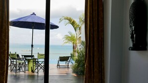 Uma área de estar ao ar livre com mesa, cadeiras, um guarda-sol azul e vista para o oceano.
