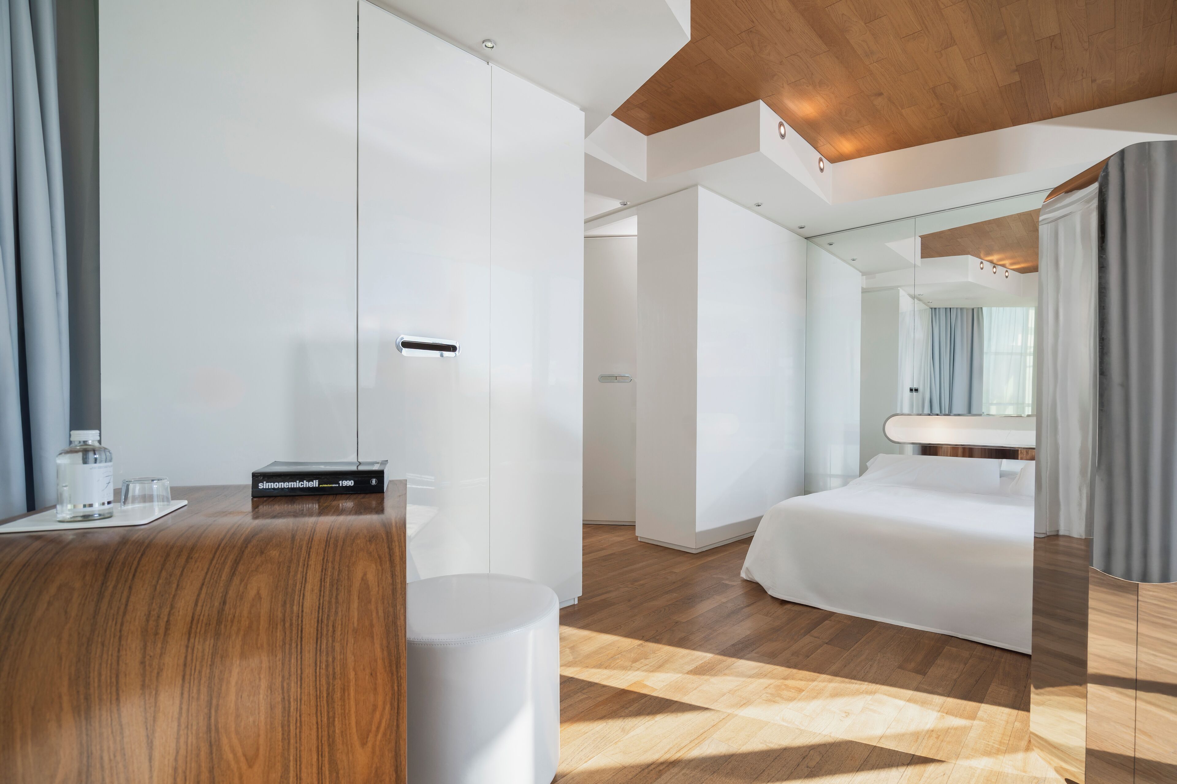 Quarto de hotel moderno com um balcão de recepção de madeira, uma cama e um espelho grande.