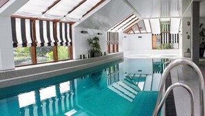 Uma piscina interior moderna com água azul cristalina, amplas janelas e área coberta com toldos listrados.
