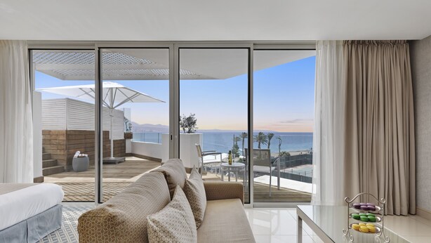 Quarto de hotel moderno com uma grande porta de vidro deslizante que dá para uma varanda com vista para o oceano.