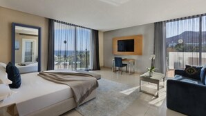 Quarto de hotel moderno com uma cama grande, escrivaninha, sofá, televisão e varanda com vista.