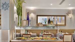 Uma área de buffet com diversos pratos, um vaso grande com folhagens e um adorno de roda de navio na parede.