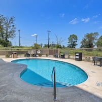 Piscina com escada de metal, cercada por uma grade, e mobiliário de exterior.