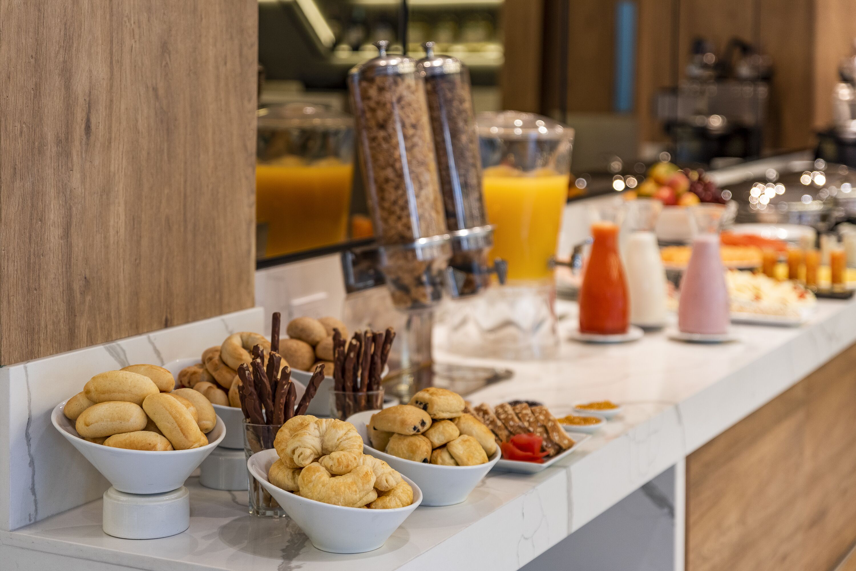 Buffet com diversas opções de comida e bebida, incluindo cestas de doces, uma variedade de frutas e um dispensador de suco.