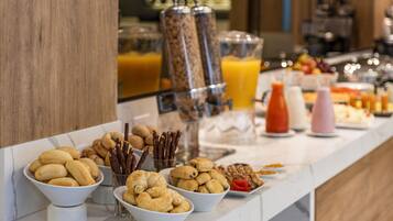 Buffet com diversas opções de comida e bebida, incluindo cestas de doces, uma variedade de frutas e um dispensador de suco.