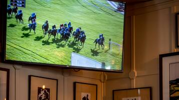 Uma televisão mostrando uma corrida de cavalos, quadros nas paredes e um sofá estampado.