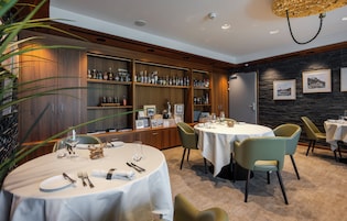 Um restaurante com mesas redondas, cadeiras e um espaço de bar com prateleiras cheias de garrafas.
