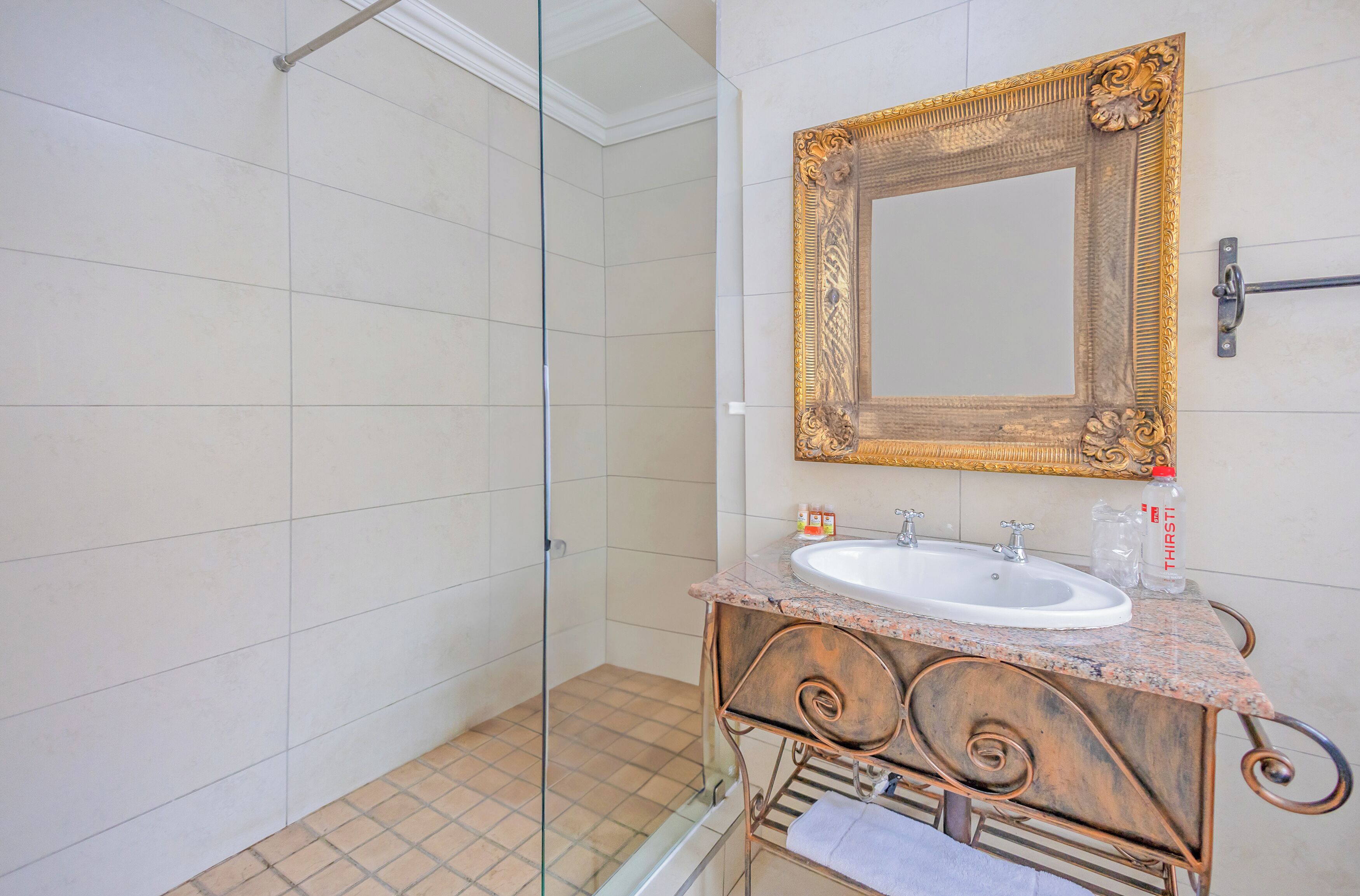 Casa de banho com cabine de chuveiro em vidro, lavatório com bancada de mármore e espelho trabalhado.