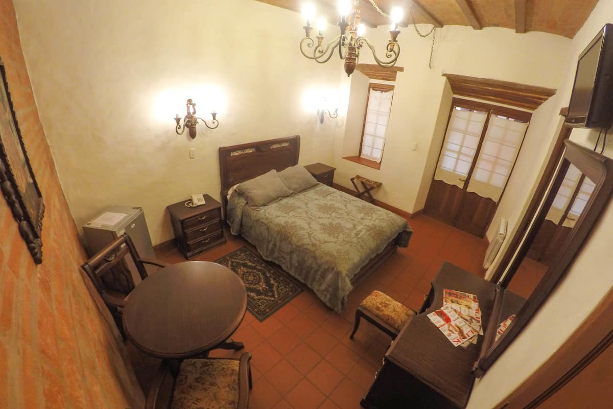Quarto com cama, mesas de cabeceira, cadeira, escrivaninha, abajur e televisão.