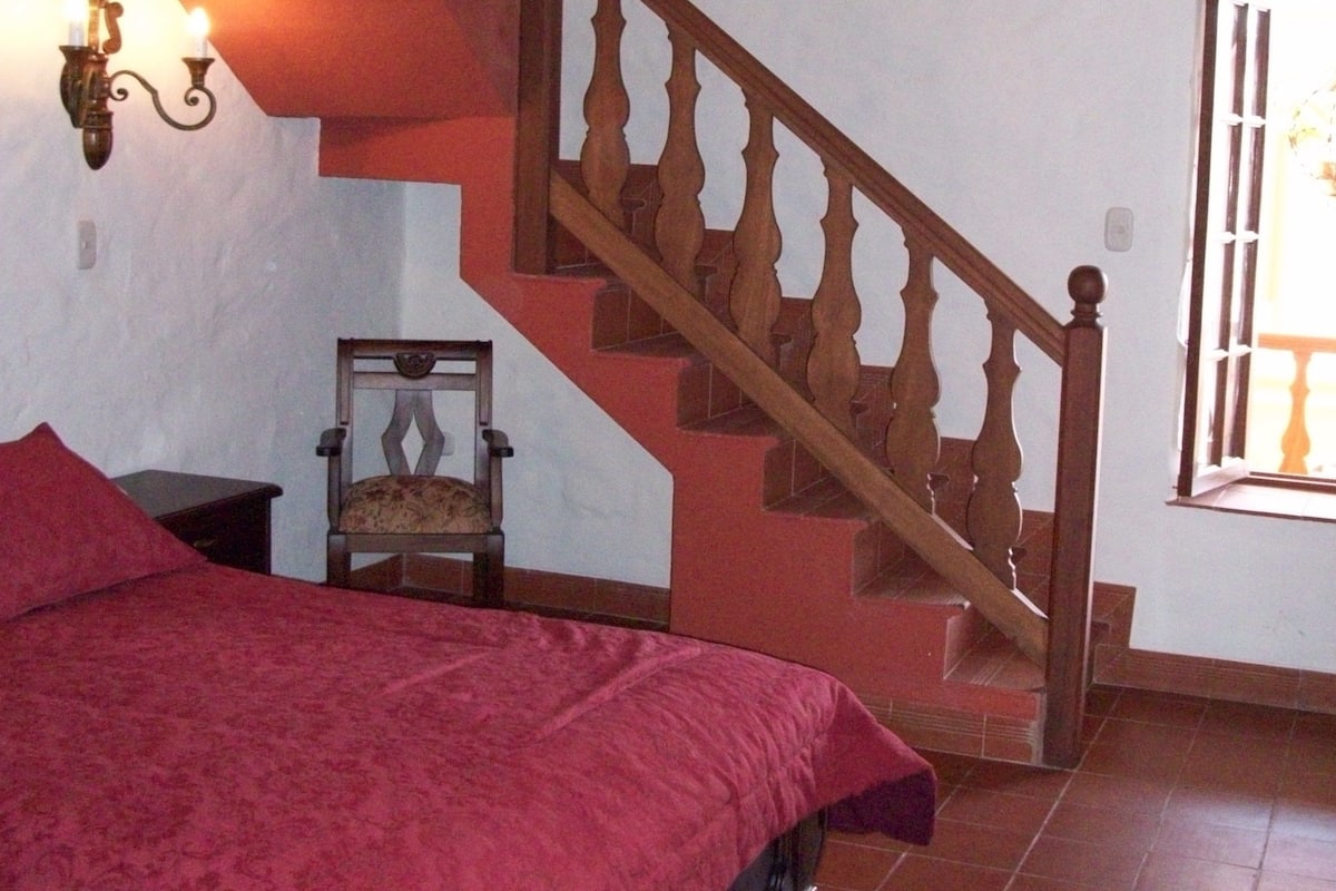 Quarto com uma cama grande, escada de madeira e uma cadeira pequena.