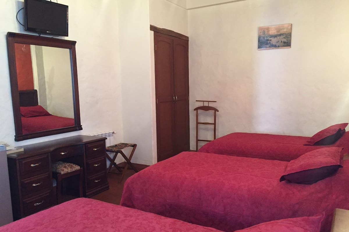 Quarto com duas camas, uma cômoda, um espelho, uma porta e uma pequena prateleira.