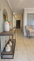 Um corredor com uma mesa comprida, uma cadeira e uma escada ao fundo.