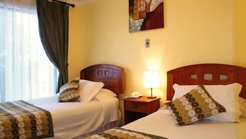 Quarto de hotel com duas camas, cada uma com colcha estampada, cabeceira de madeira, luminária de cabeceira e um quadro na parede.